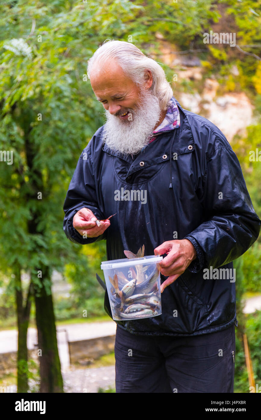 Positive gray-haired fisherman with his small catch smiling Stock Photo ...