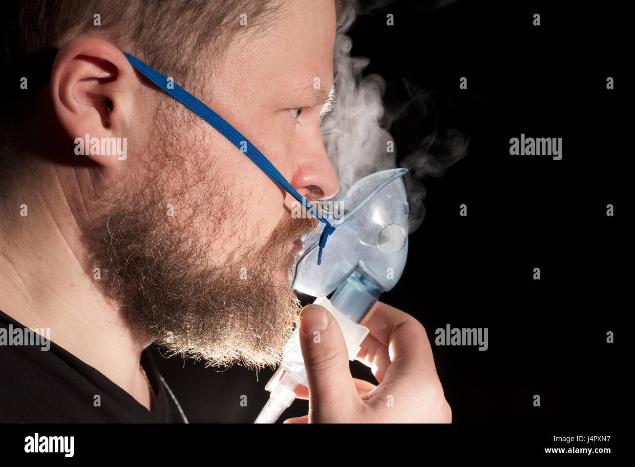 Man breathing through nebulizer mask on black background Stock Photo ...