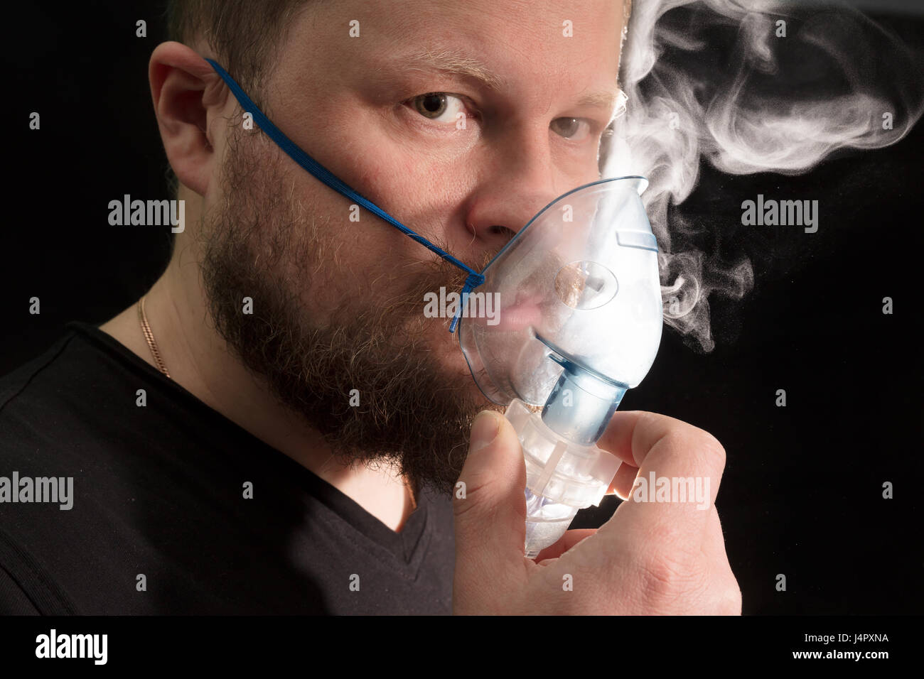 Man breathing through nebulizer mask on black background Stock Photo ...