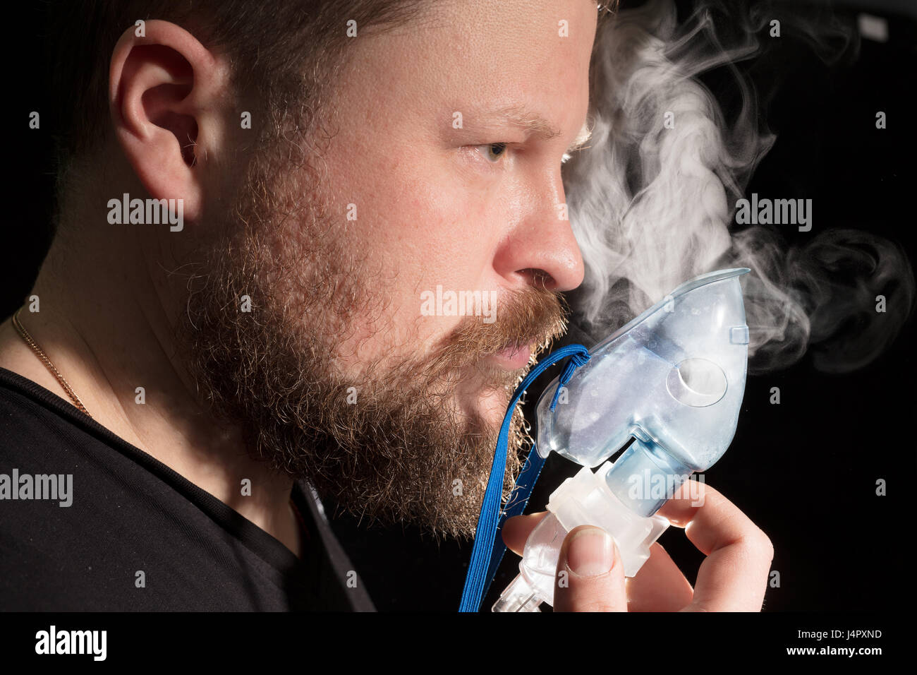 Man breathing through nebulizer mask on black background Stock Photo ...