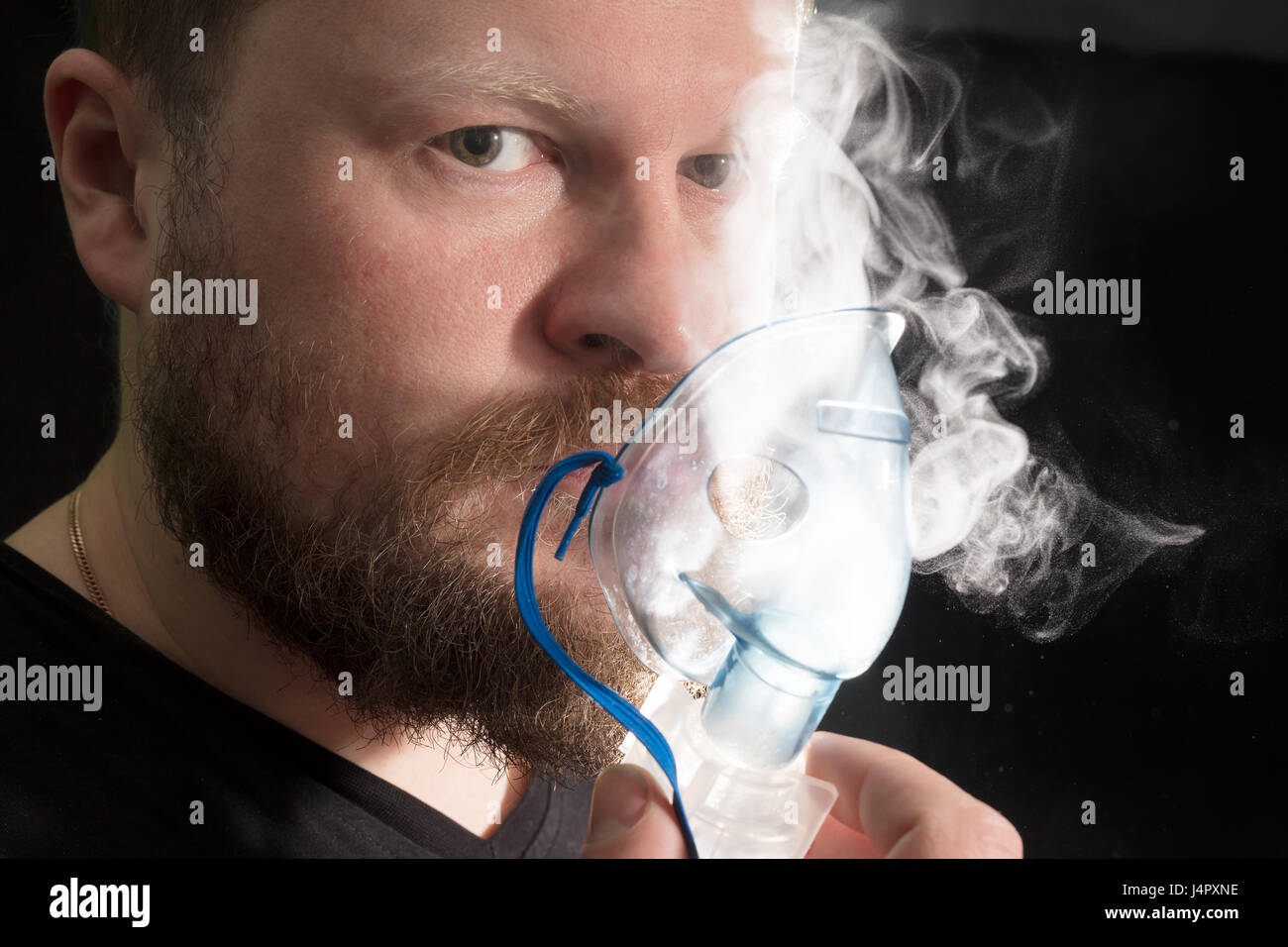 Man breathing through nebulizer mask on black background Stock Photo ...