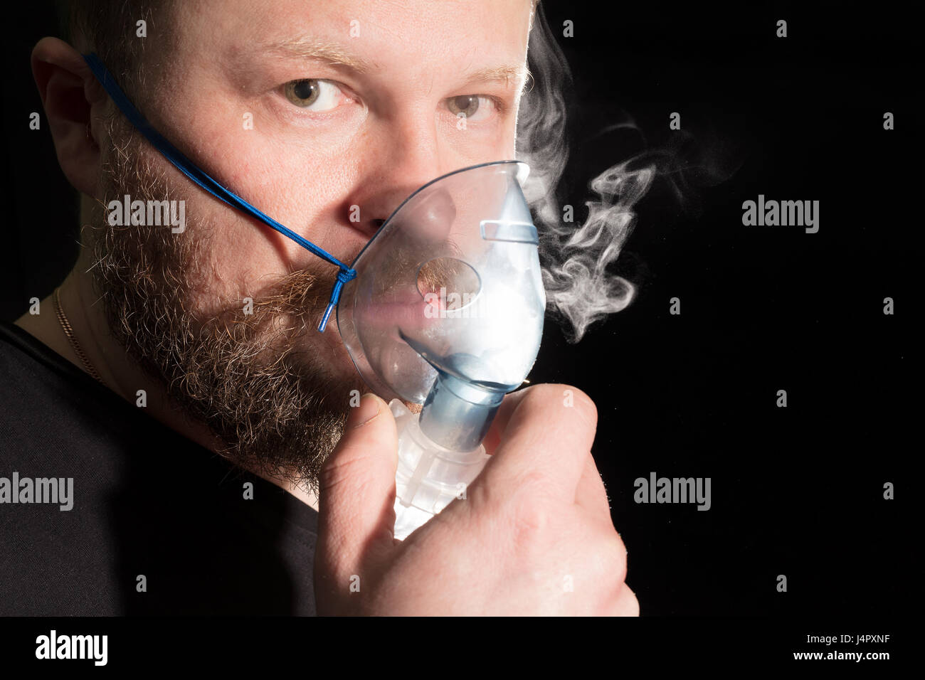 Man breathing through nebulizer mask on black background Stock Photo ...