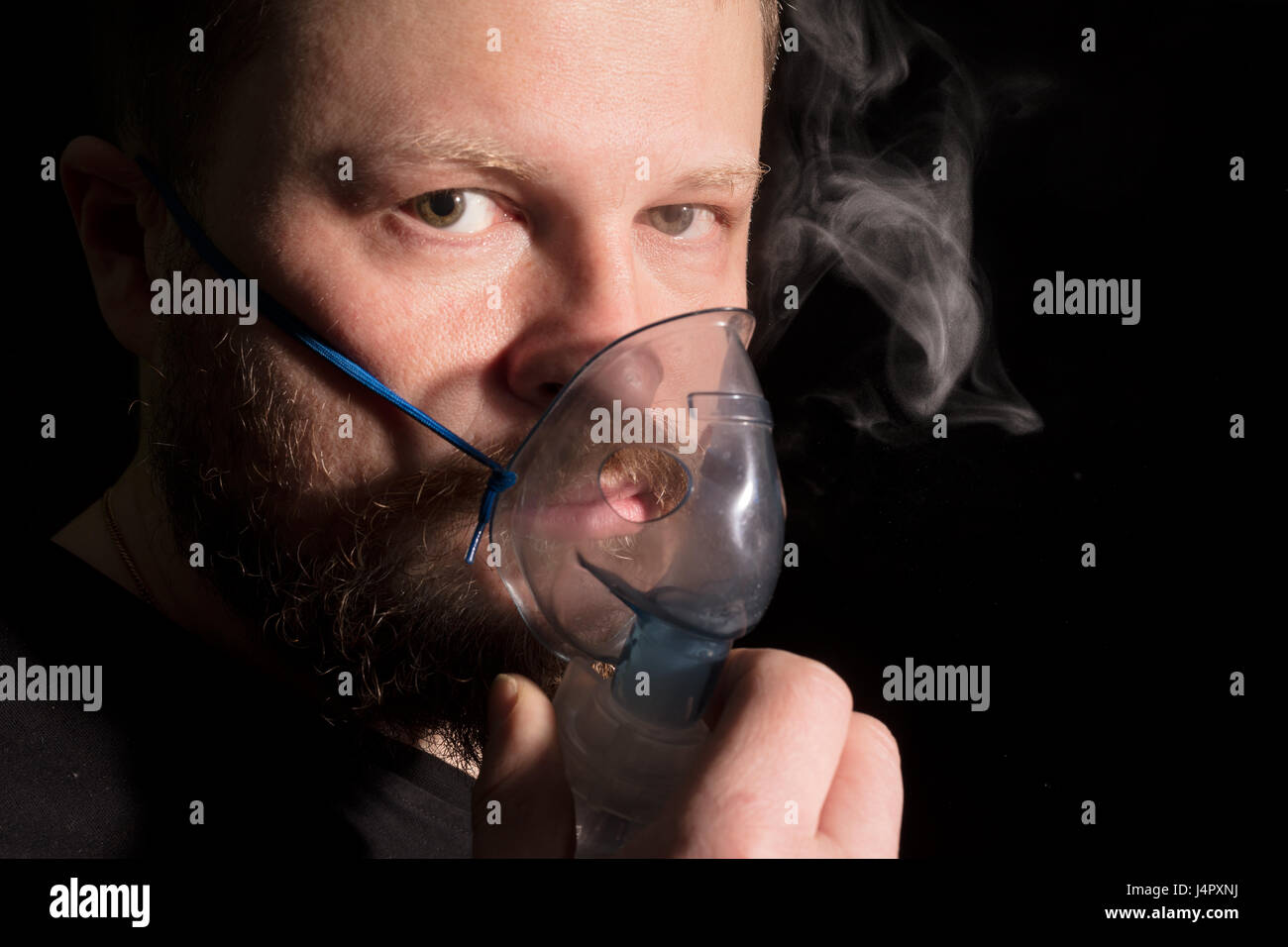 Man breathing through nebulizer mask on black background Stock Photo ...