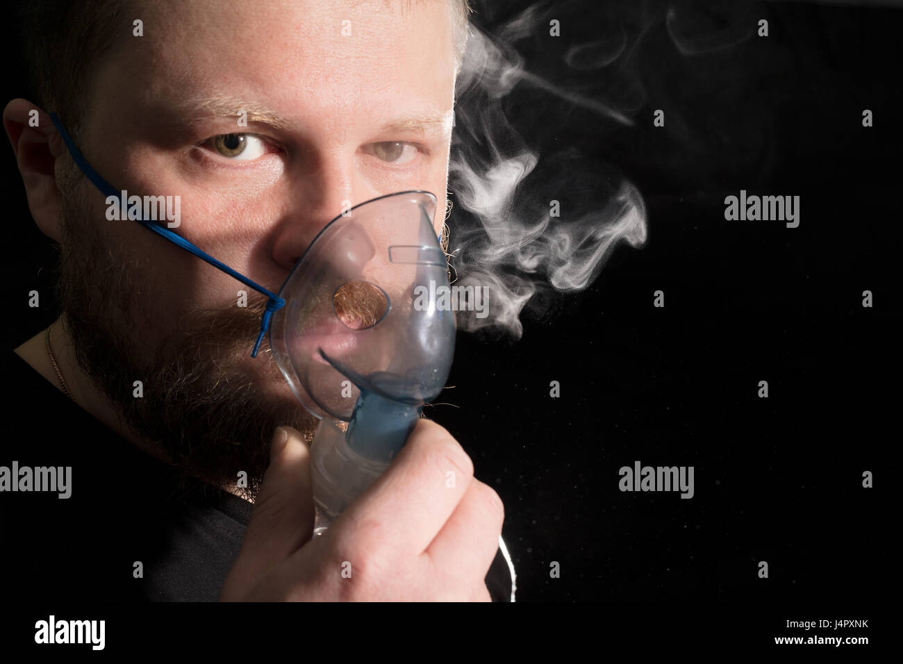 Man breathing through nebulizer mask on black background Stock Photo ...