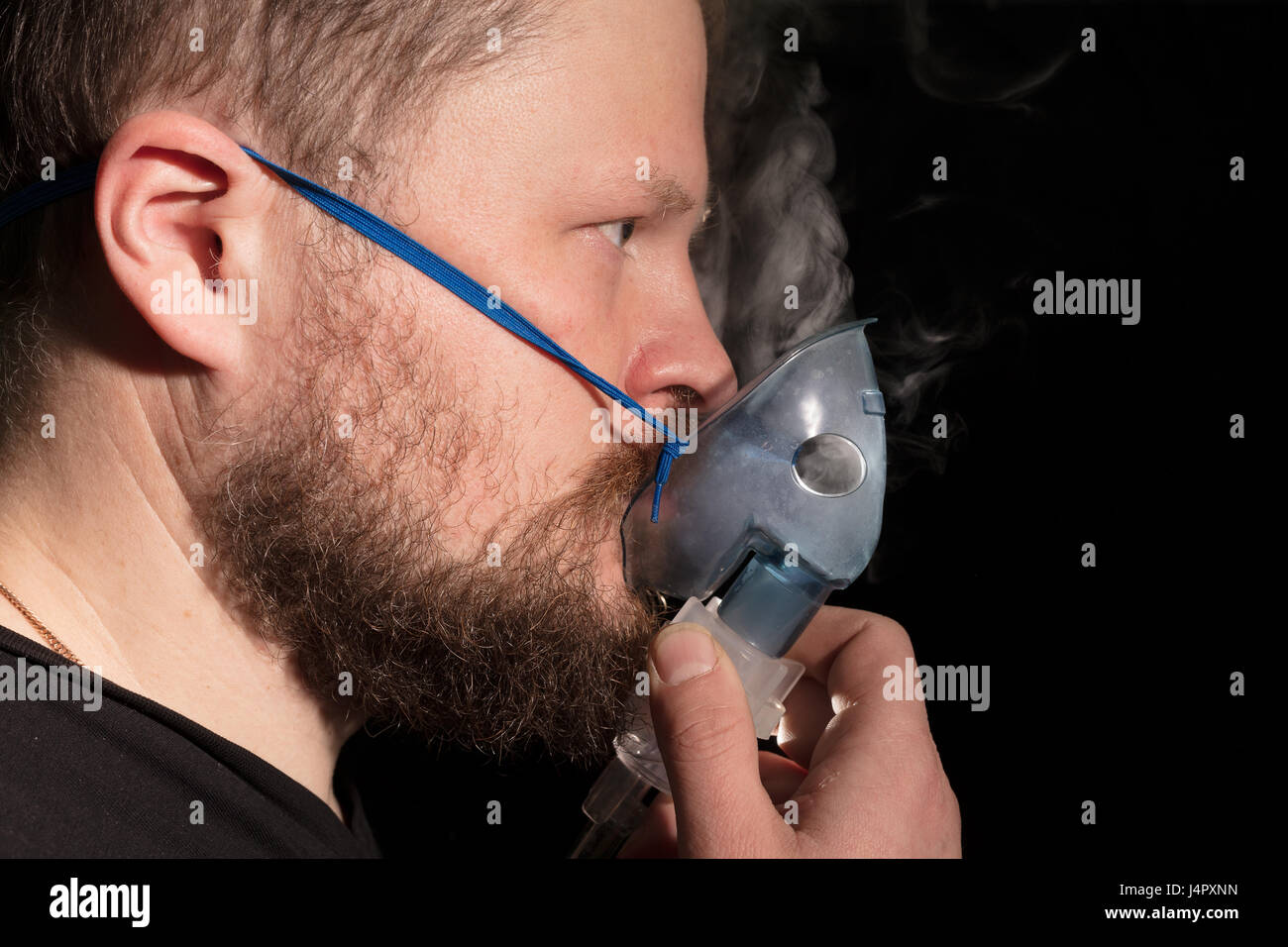 Man breathing through nebulizer mask on black background Stock Photo ...