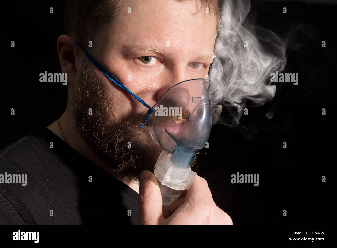 Man breathing through nebulizer mask on black background Stock Photo ...
