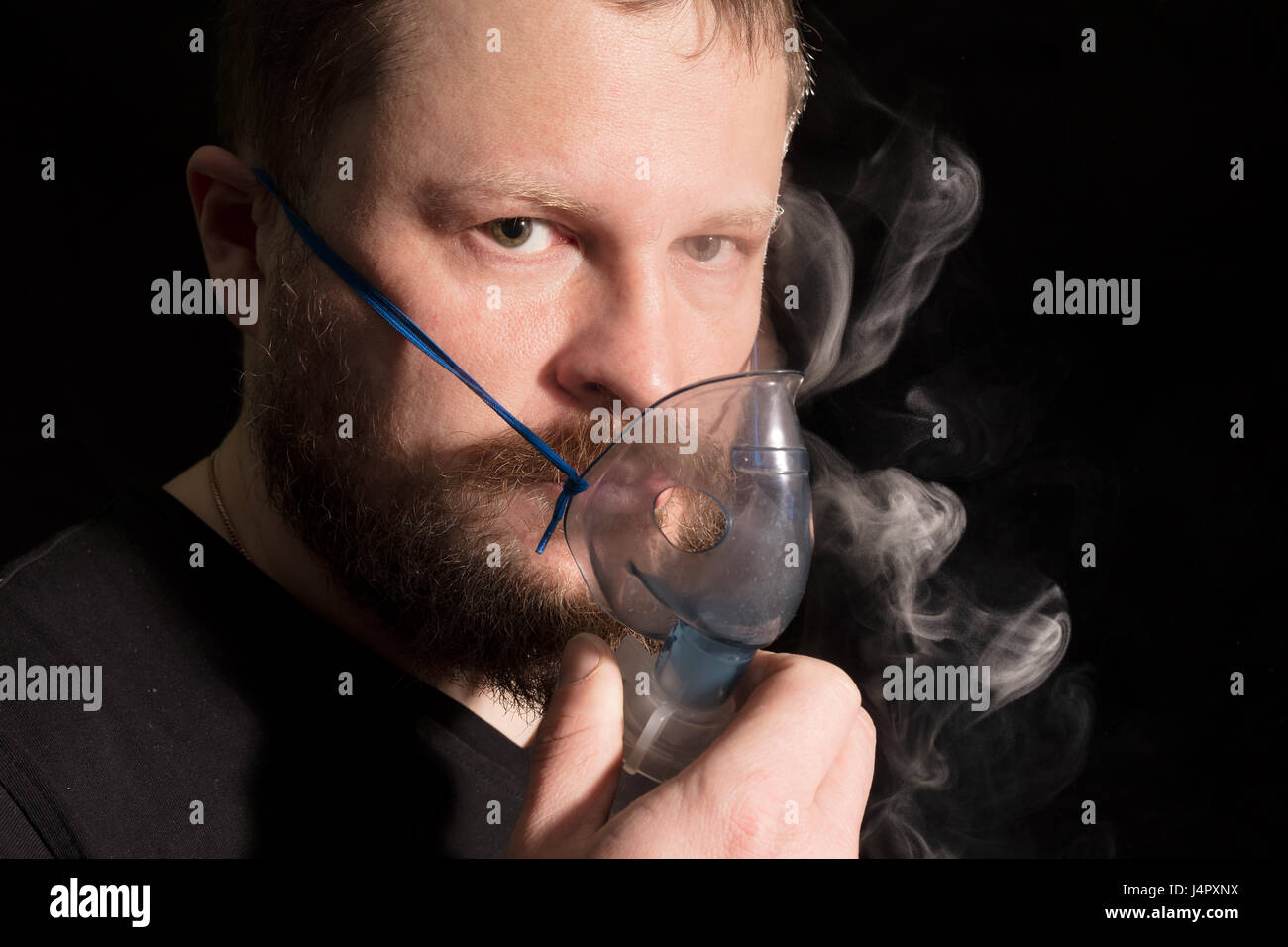 Man breathing through nebulizer mask on black background Stock Photo ...