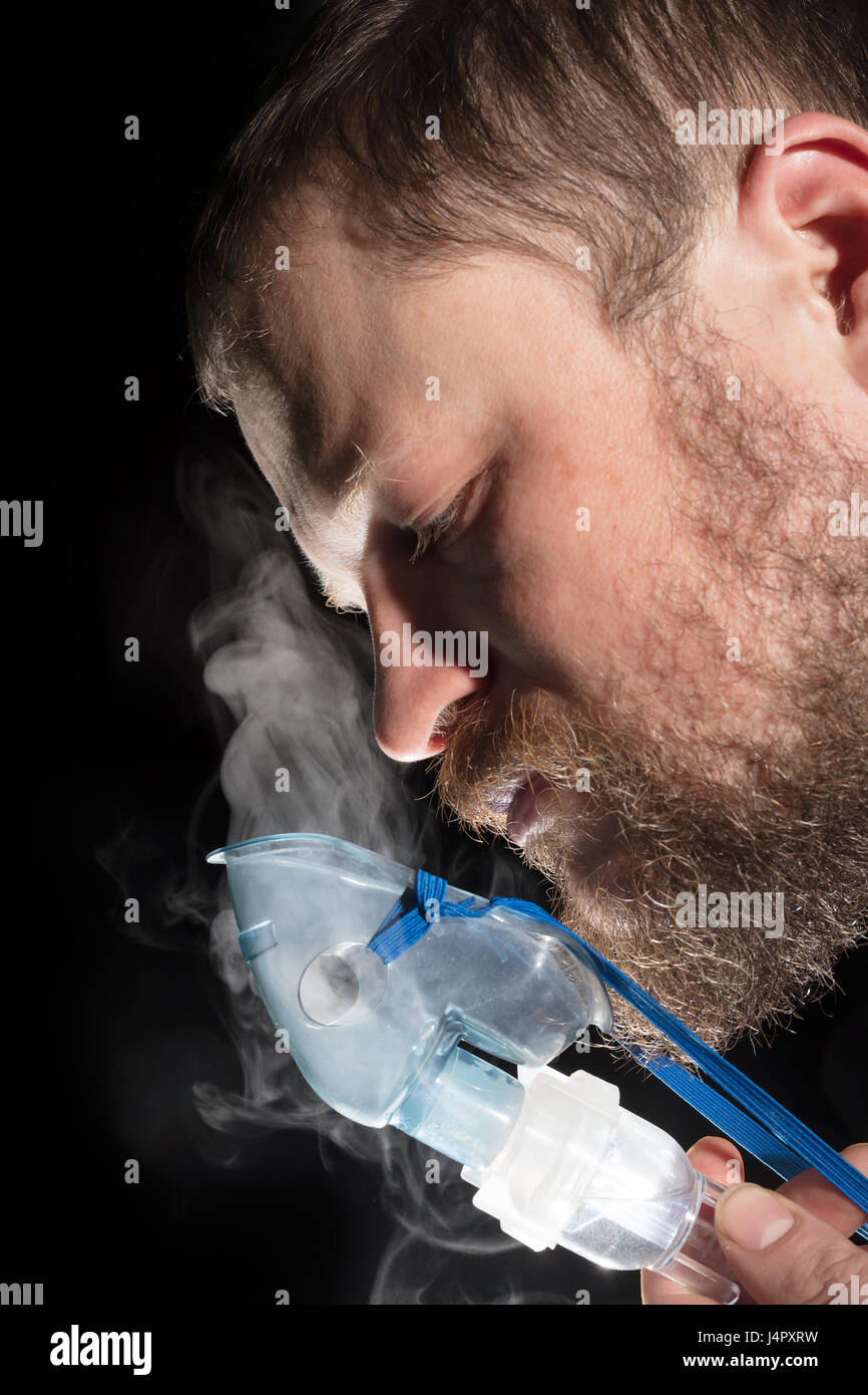 Man breathing through nebulizer mask on black background Stock Photo ...