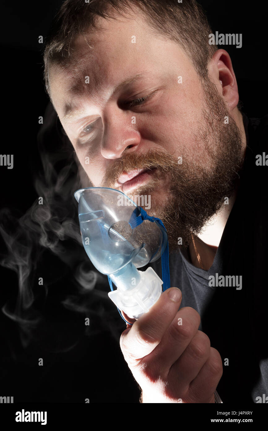 Man breathing through nebulizer mask on black background Stock Photo ...