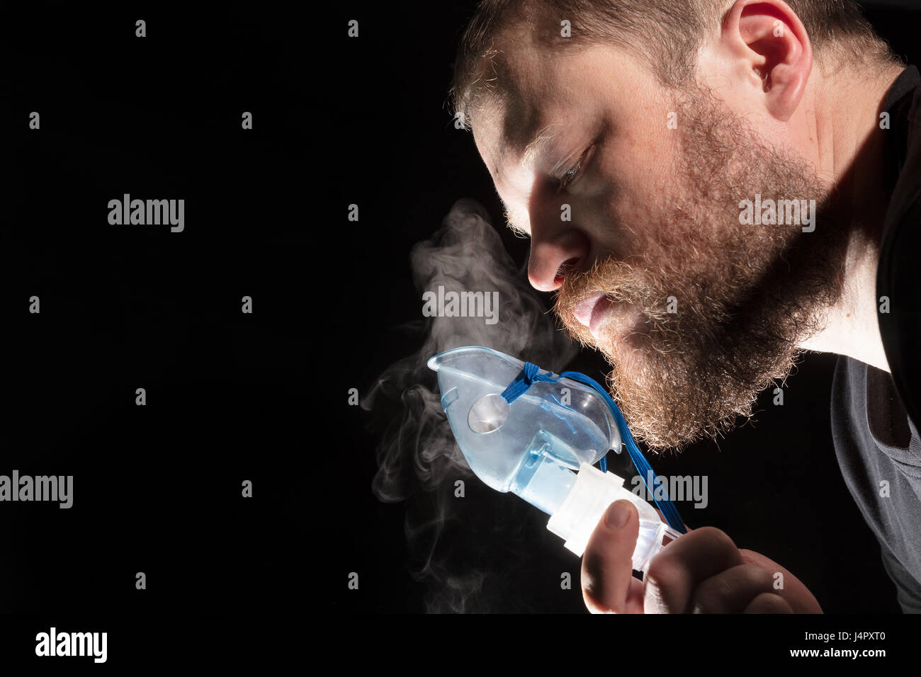 Man breathing through nebulizer mask on black background Stock Photo ...