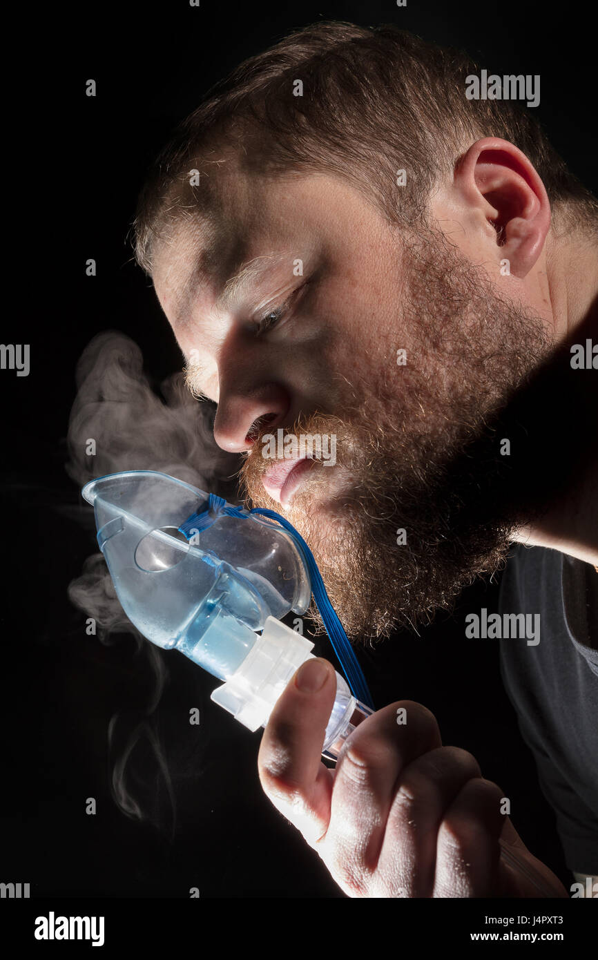 Man breathing through nebulizer mask on black background Stock Photo ...