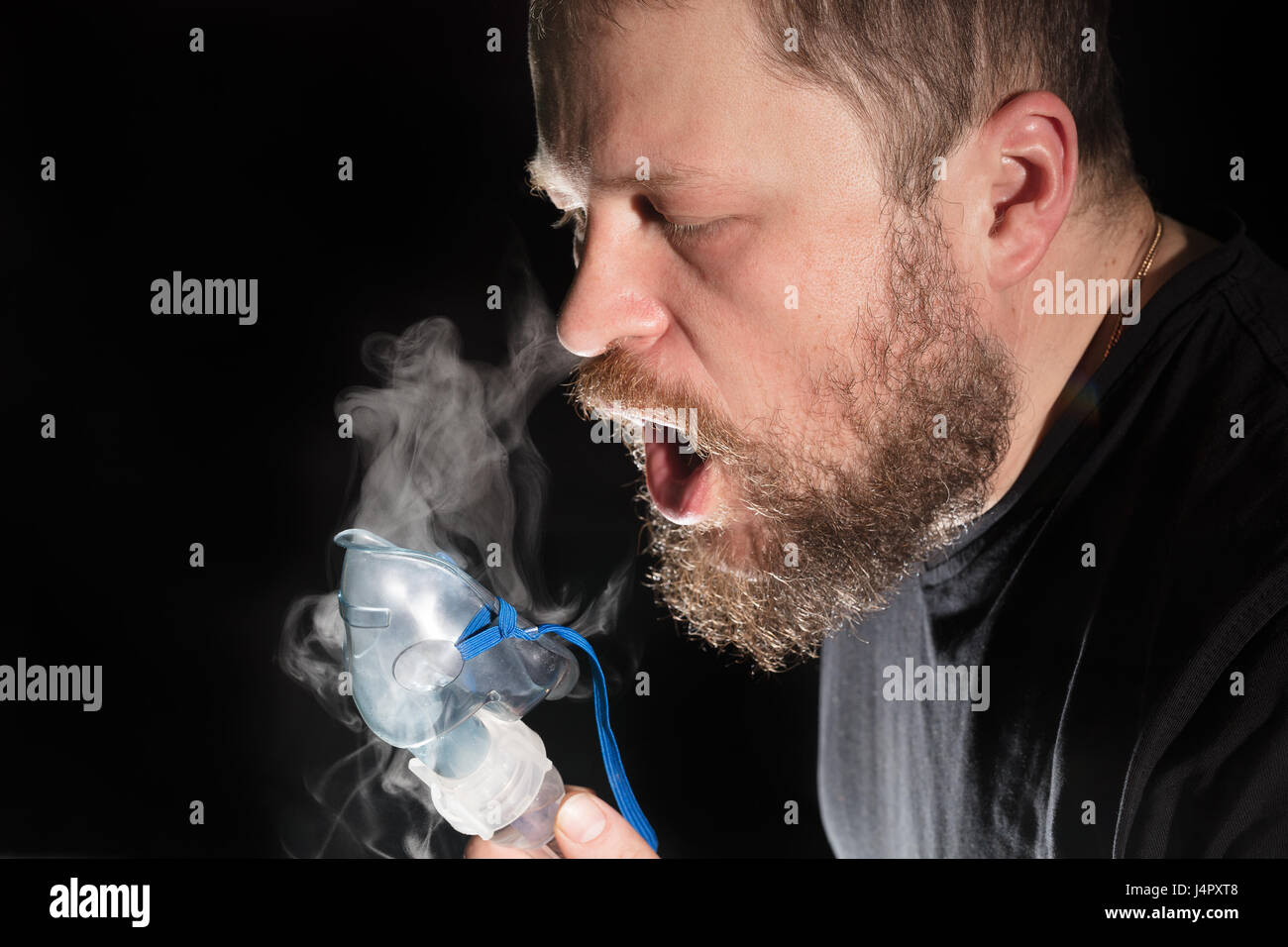 Man breathing through nebulizer mask on black background Stock Photo ...