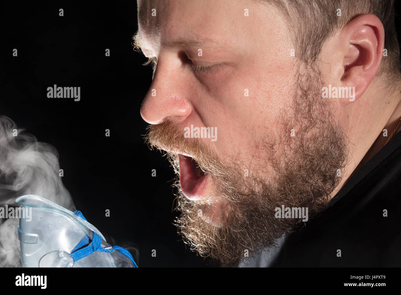 Man breathing through nebulizer mask on black background Stock Photo ...
