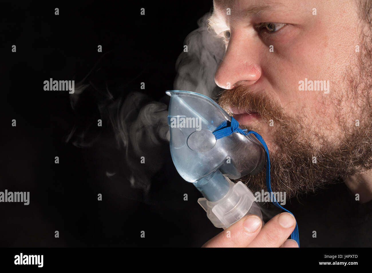 Man breathing through nebulizer mask on black background Stock Photo ...