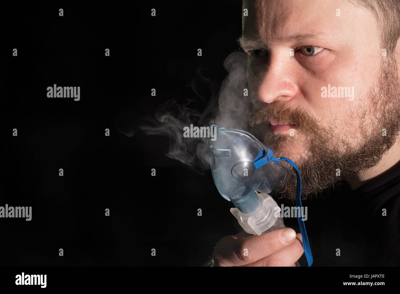 Man breathing through nebulizer mask on black background Stock Photo ...