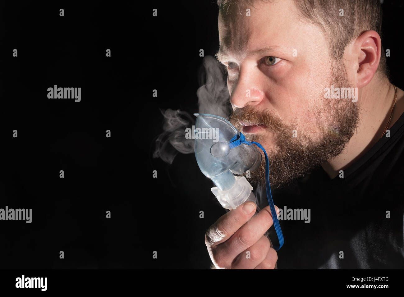 Man breathing through nebulizer mask on black background Stock Photo ...