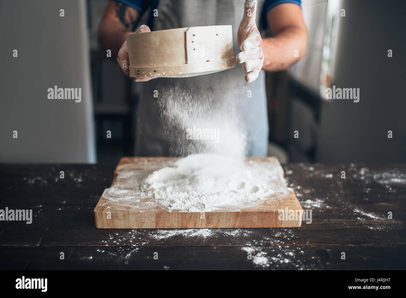 Male baker hands filters the flour through a sieve over cutting board ...