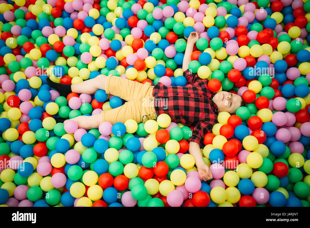 Little boy lying in a pile of colorful inflatable balloons in childrens ...