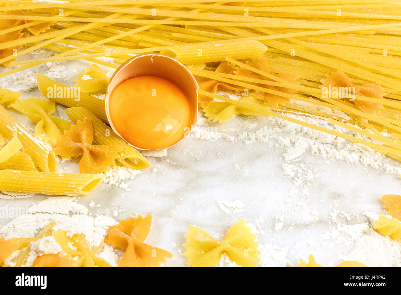 A closeup of an egg among various types of pasta, on a white marble ...