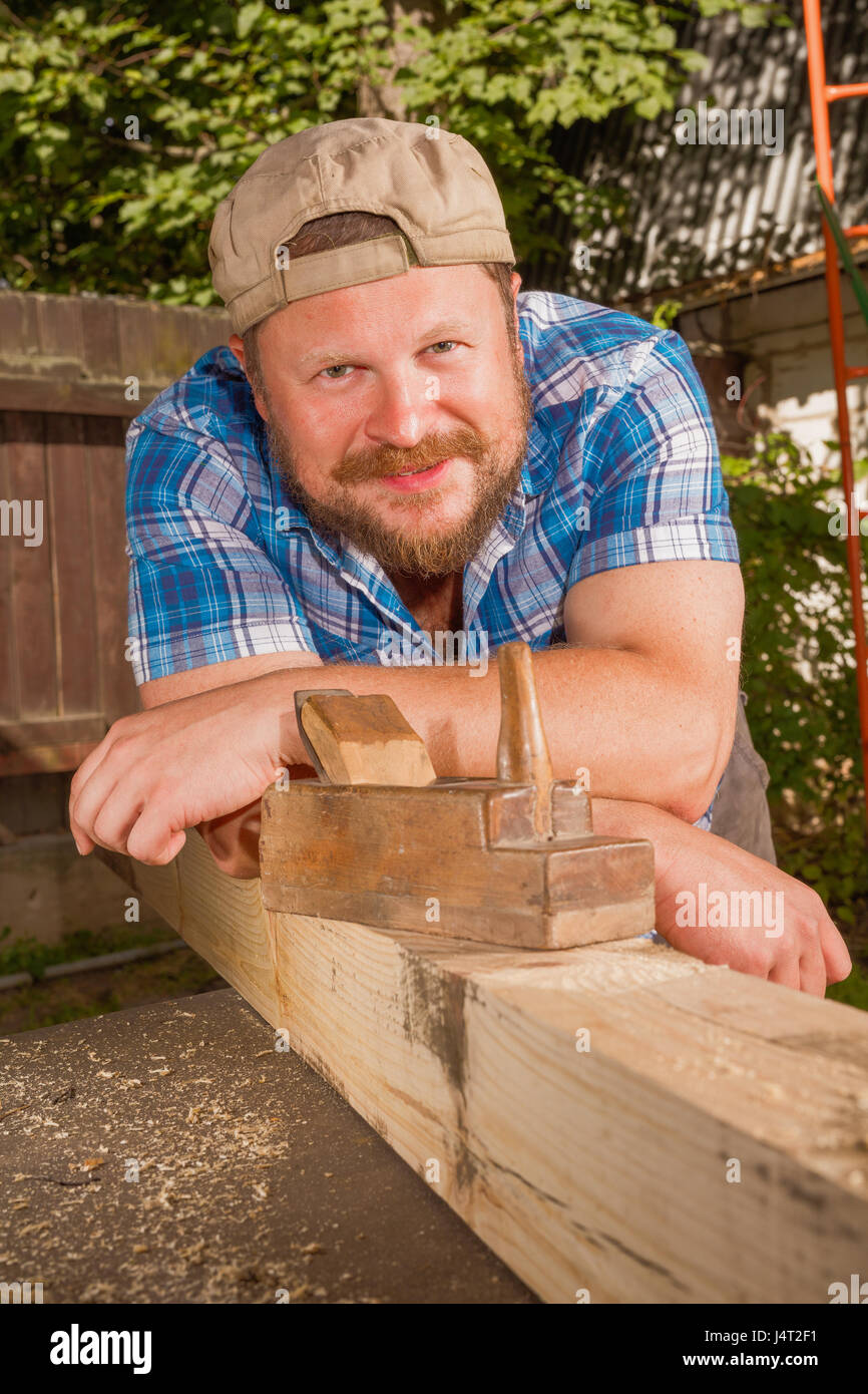 Carprnter's portrait with wooden plank and plane smiling on natural ...