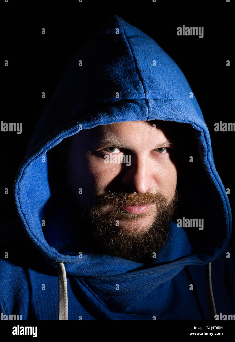 Solid bearded middle-aged man in a hood portrait on black background ...