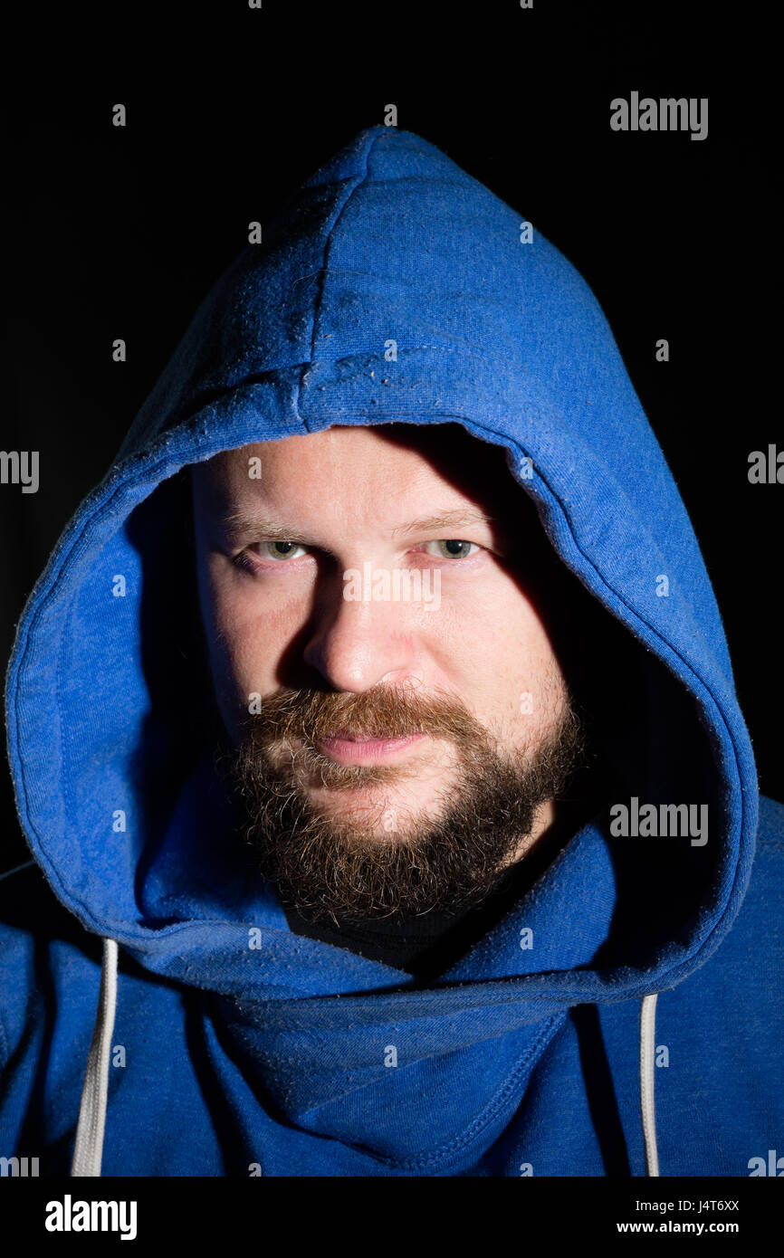 Solid bearded middle-aged man in a hood portrait on black background ...