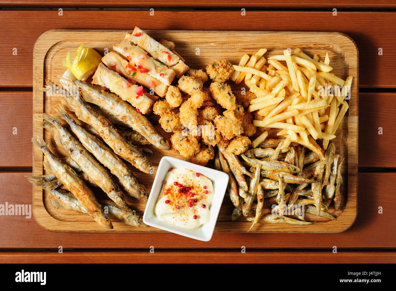 big wooden board with fried fush, mussels, french fries served as ...