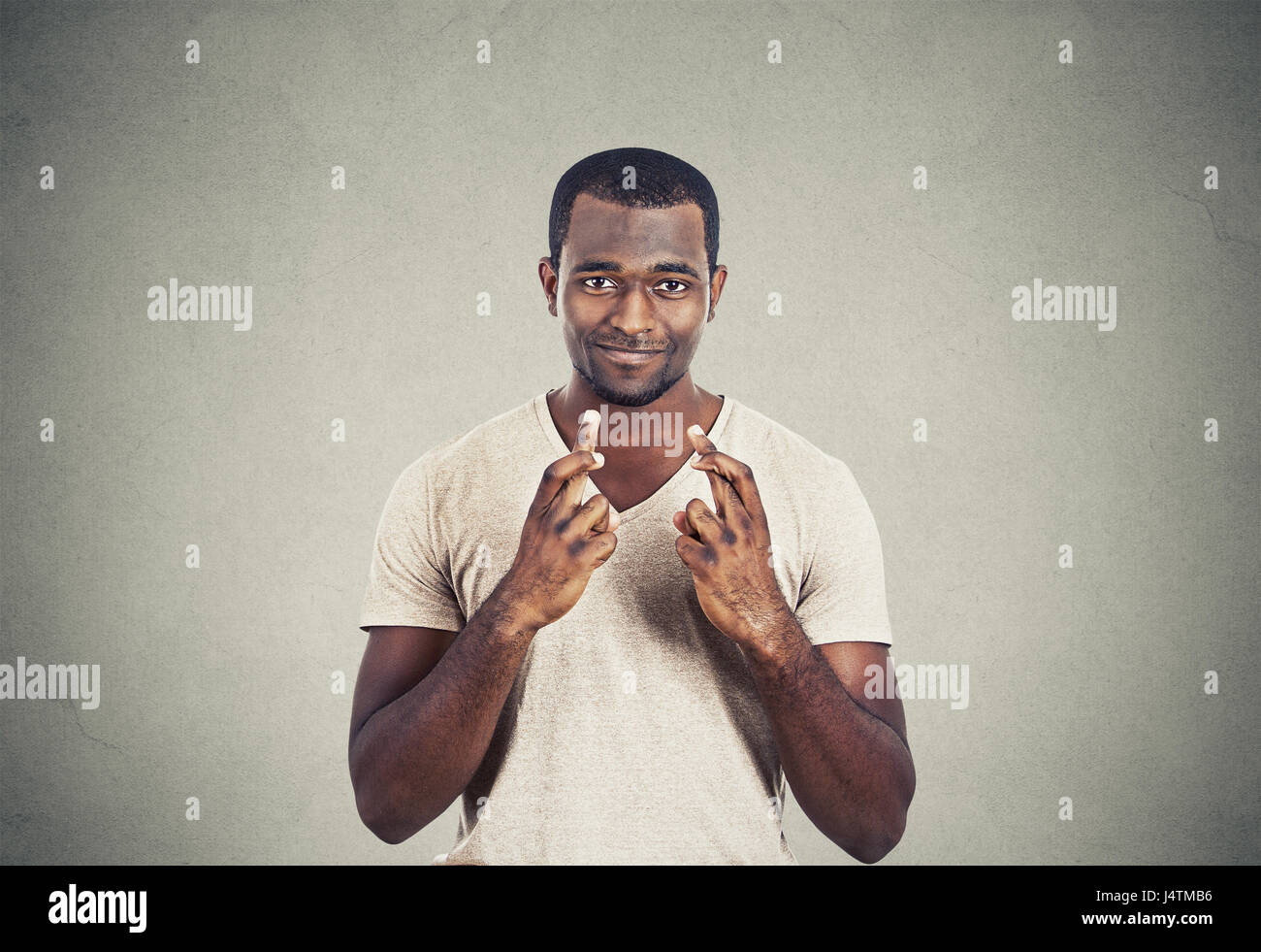 Young hopeful man crossing fingers isolated on grey wall background ...
