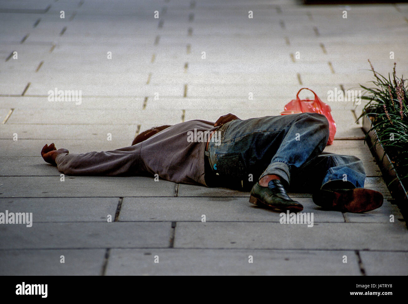 A homeless person has passed out and is laying on the sidewalk in ...