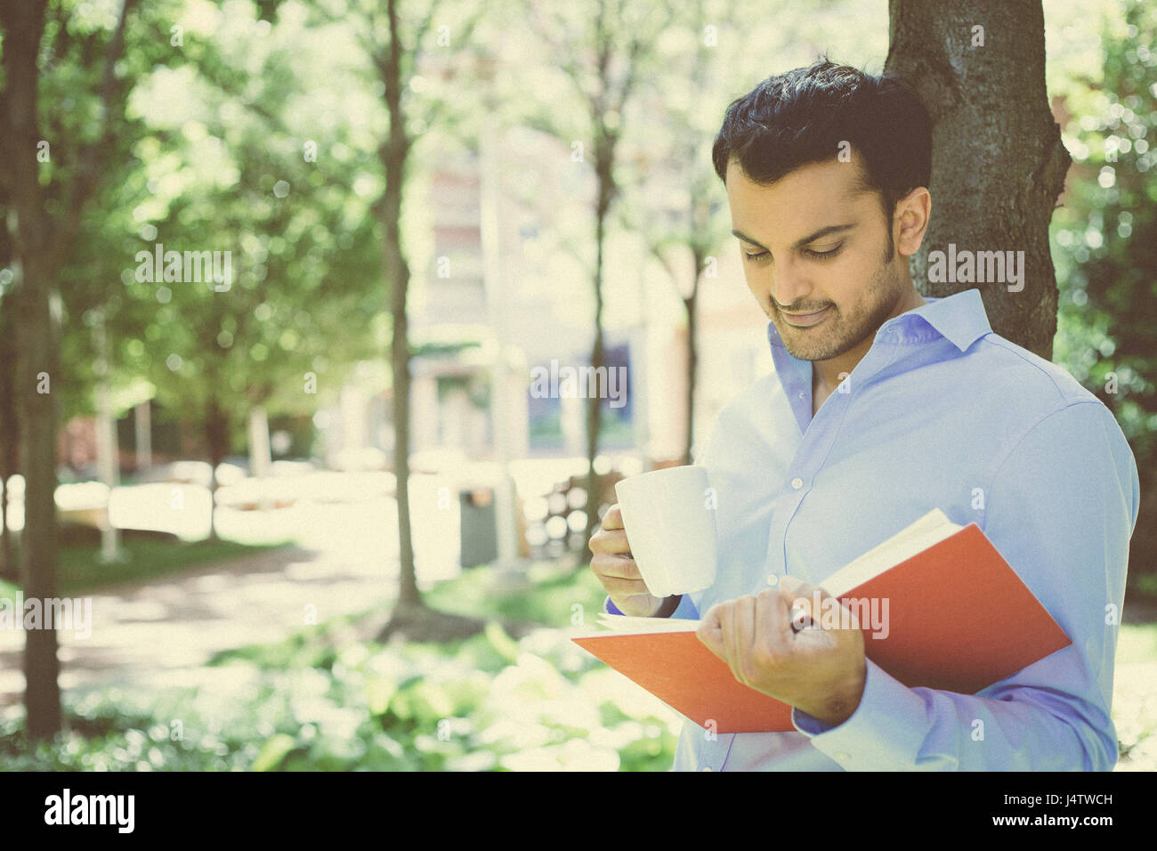 Closeup portrait young business man reading red book and drinking from ...