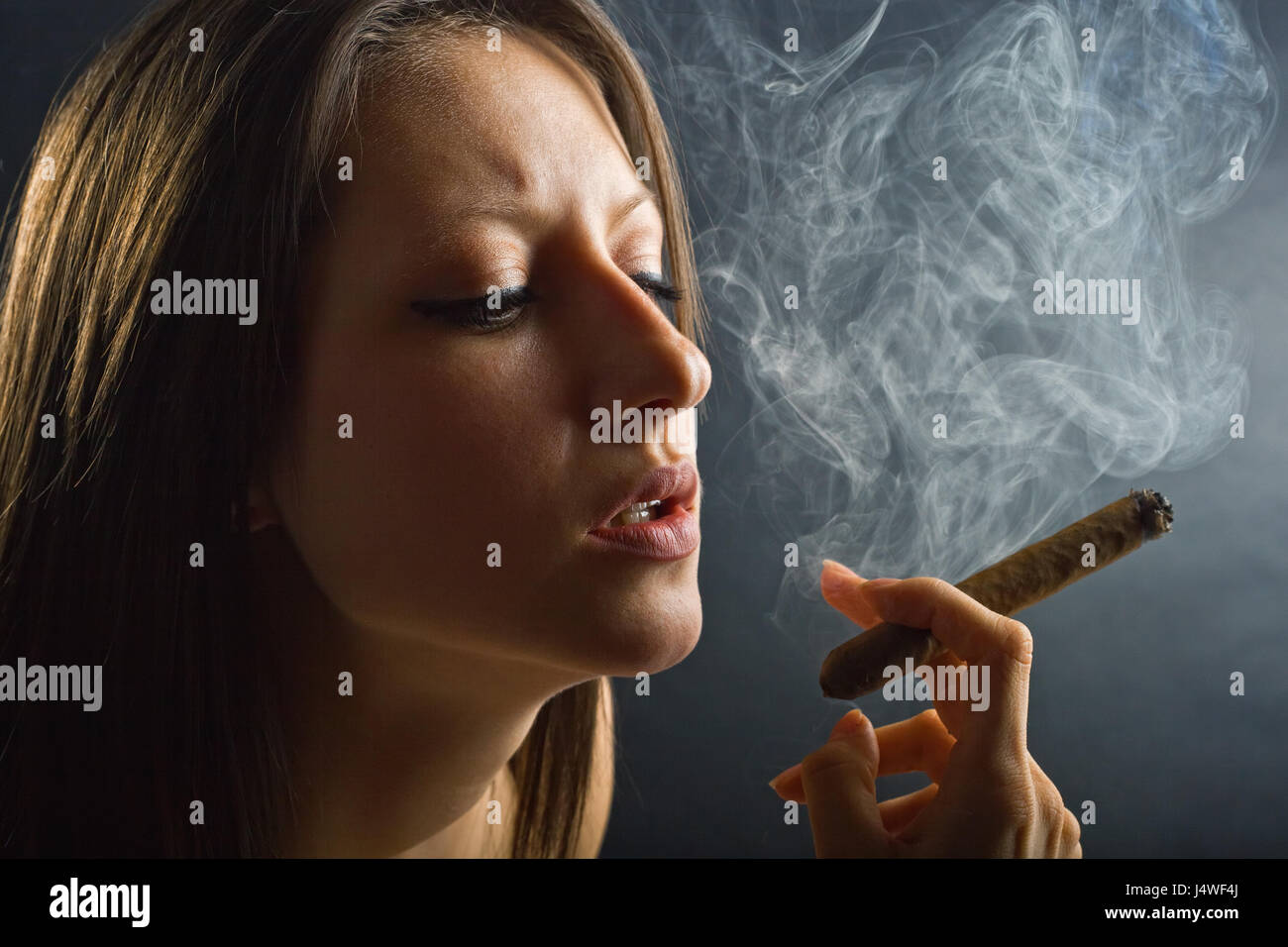 Woman with cigar exhaling smoke on a dark background Stock Photo - Alamy