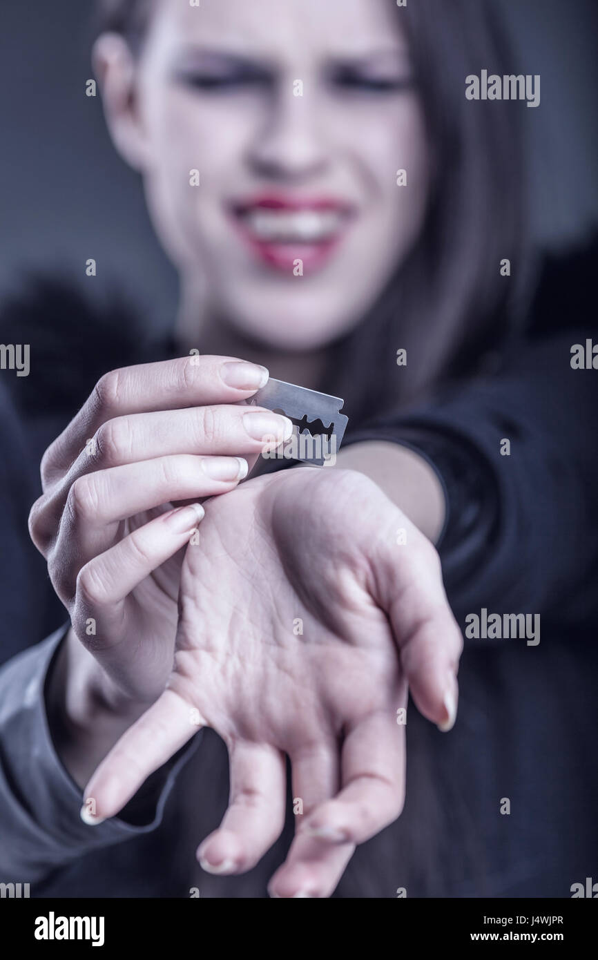 Young woman cuts veins on a hand on a dark background. Focus on hand ...