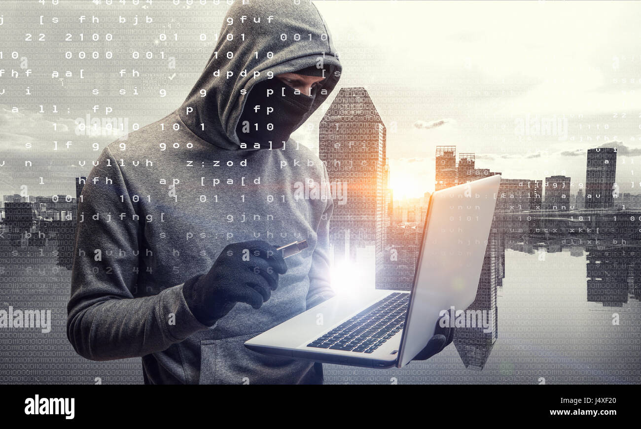 Computer hacker in hoodie and mask stealing data from laptop. Mixed ...