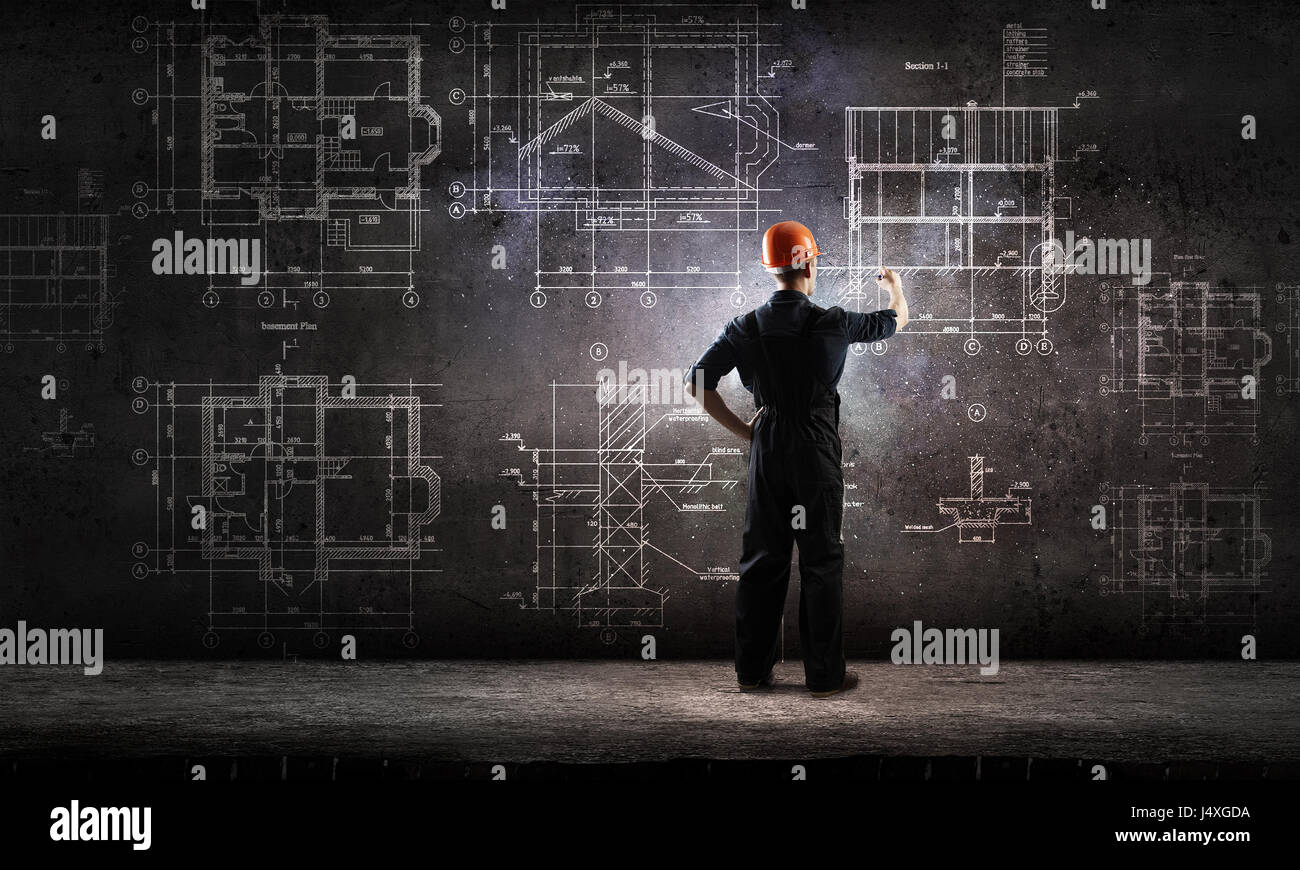 Rear view of engineer man in helmet and overall sketching construction ...