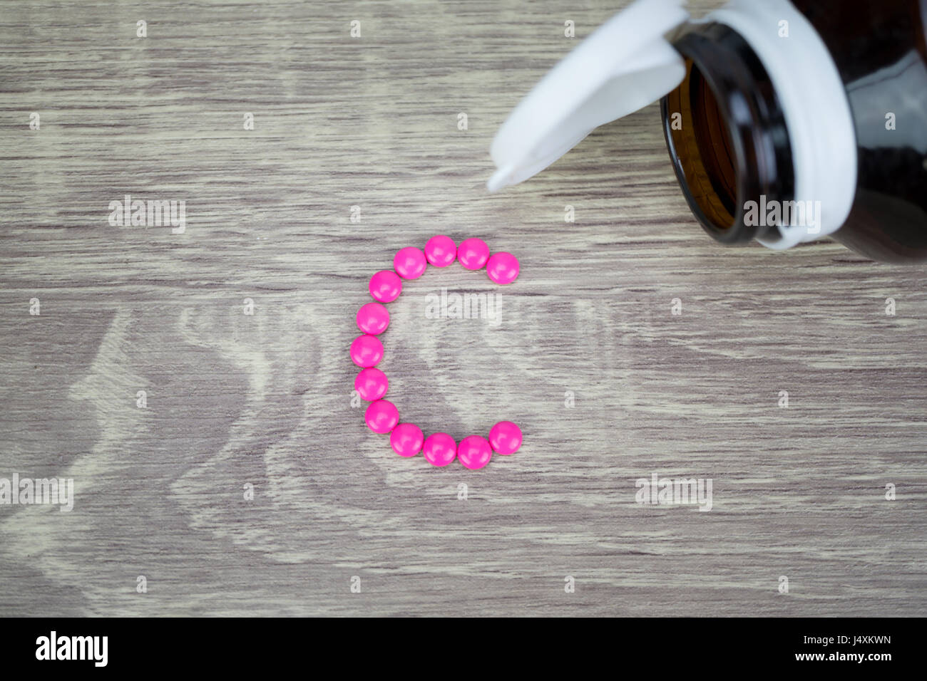 Pink pills forming shape to C alphabet on wood background Stock Photo ...