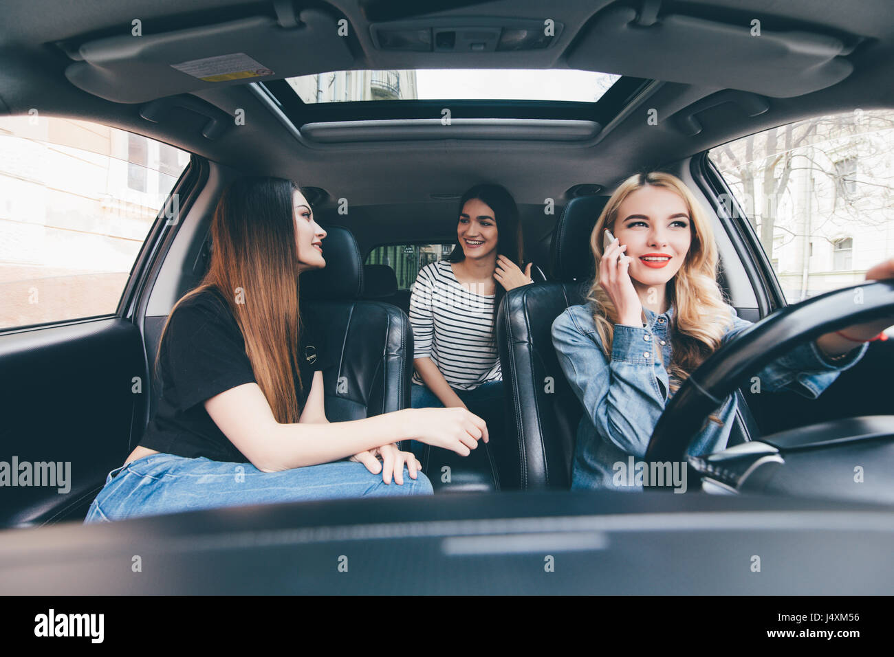 Three beautiful young women friends spend time together in the o car as ...