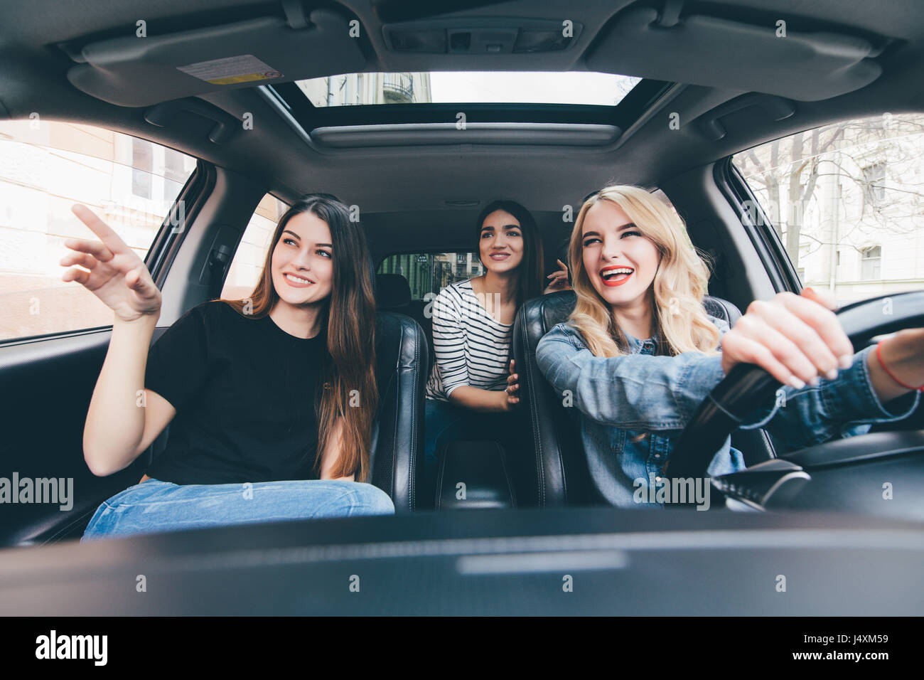 Three young cheerful women looking at pointed hand direction with smile ...