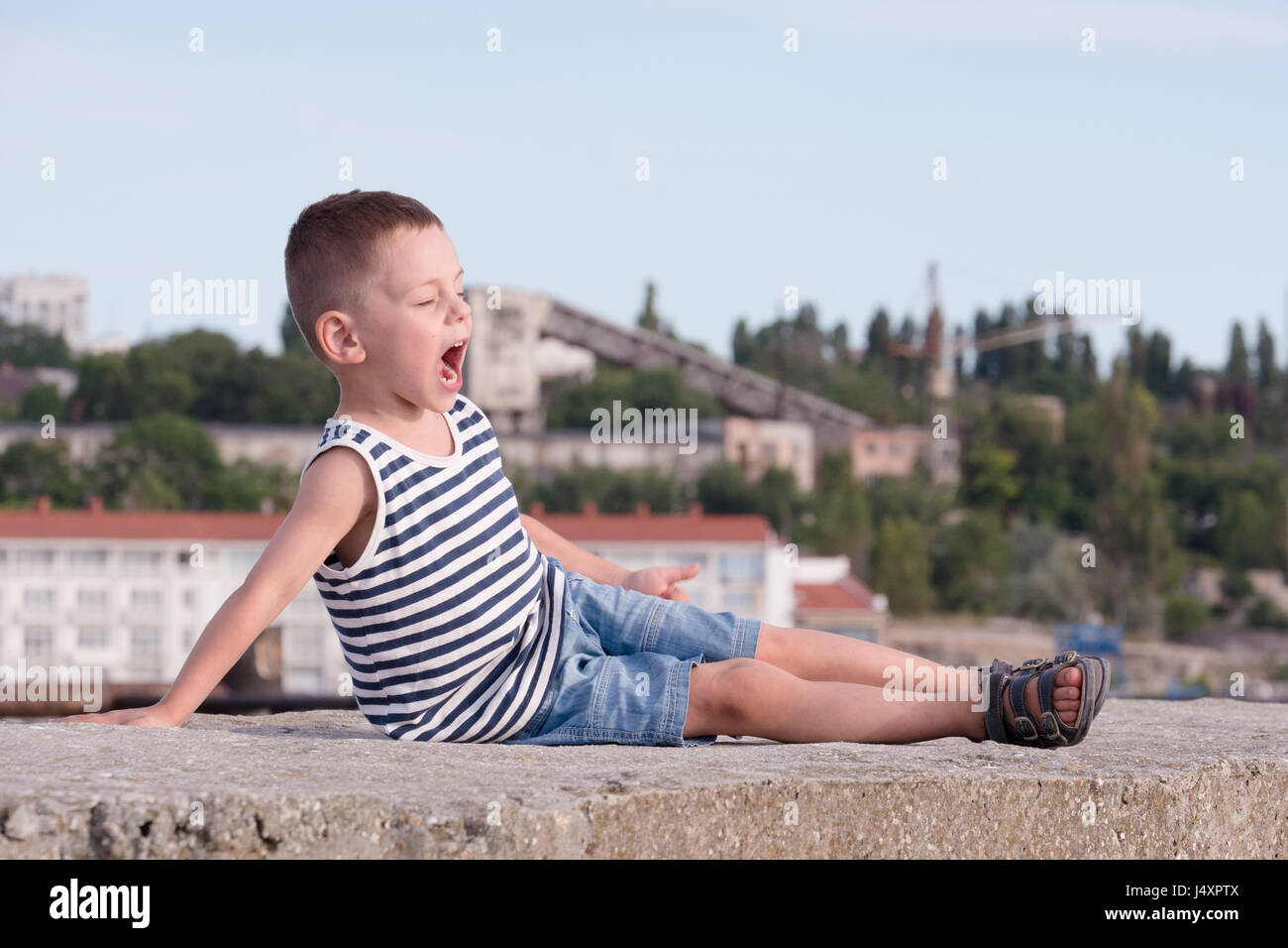 shouting little boy in shorts and sailor singlet sitting on port ...