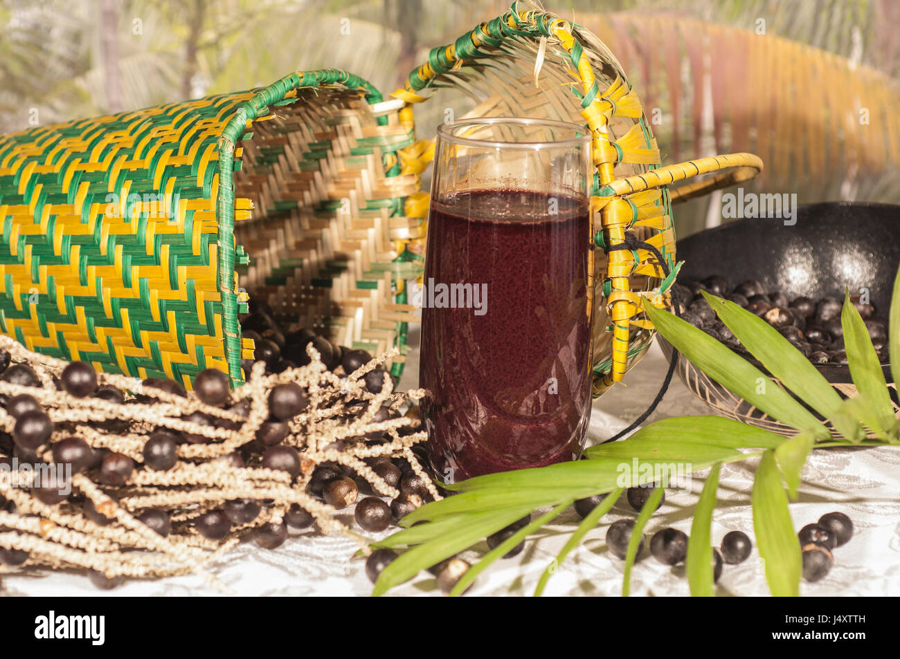 Still life image of a glass of acai wine with acai leaves, fruit, and a ...