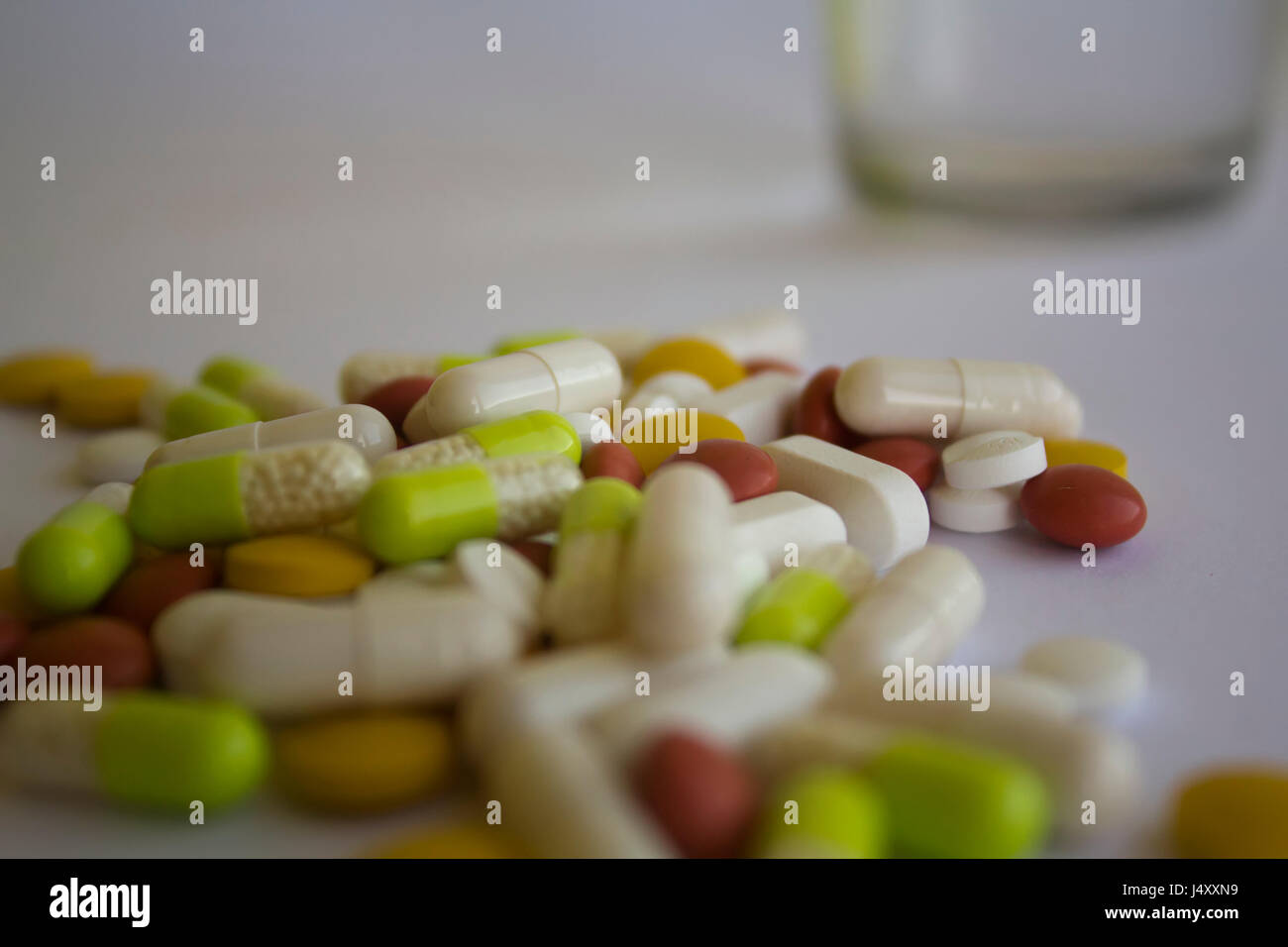 Pile of different color pills and a glass of water Stock Photo - Alamy