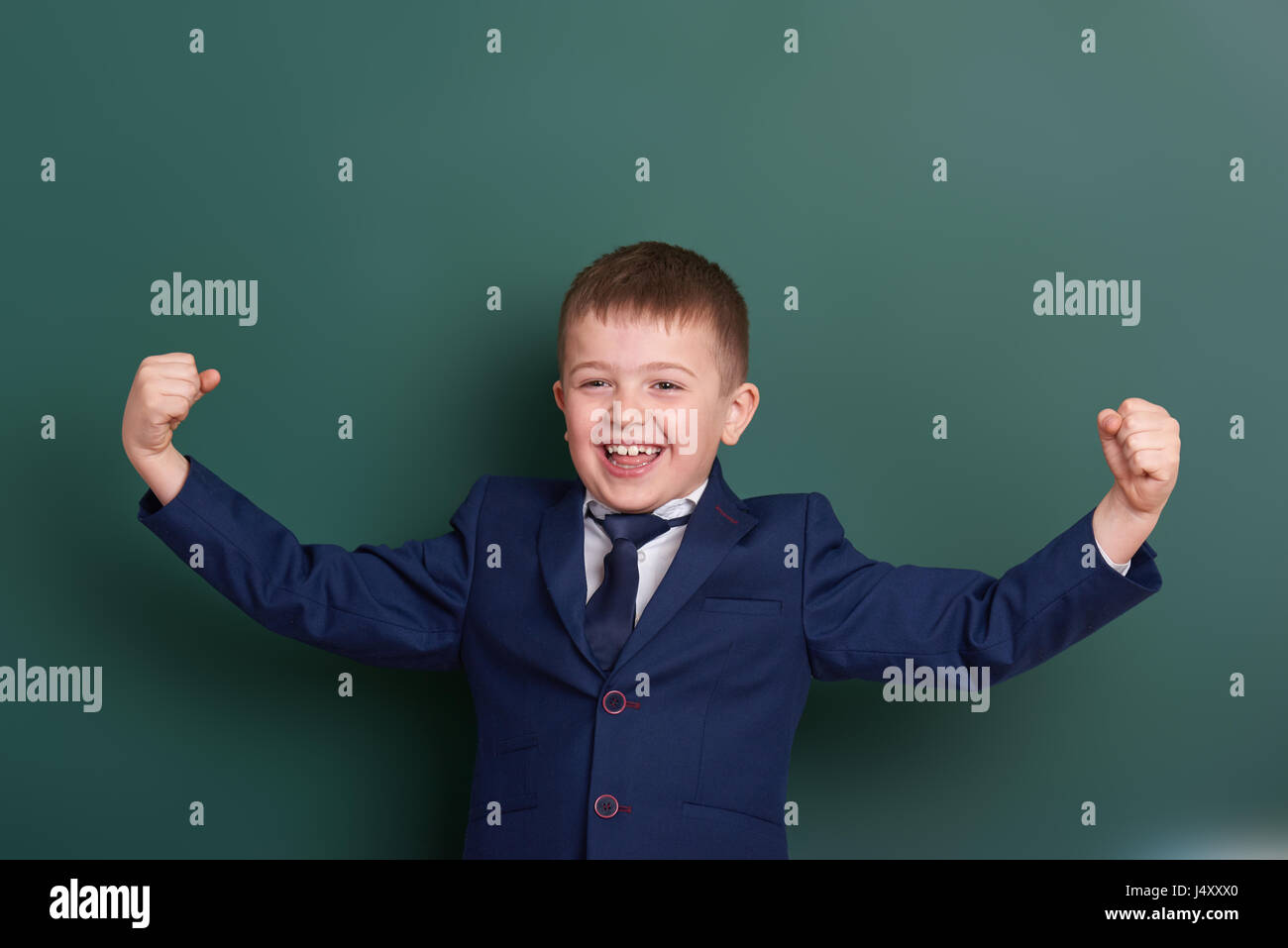 school boy show biceps muscles, portrait near green blank chalkboard ...