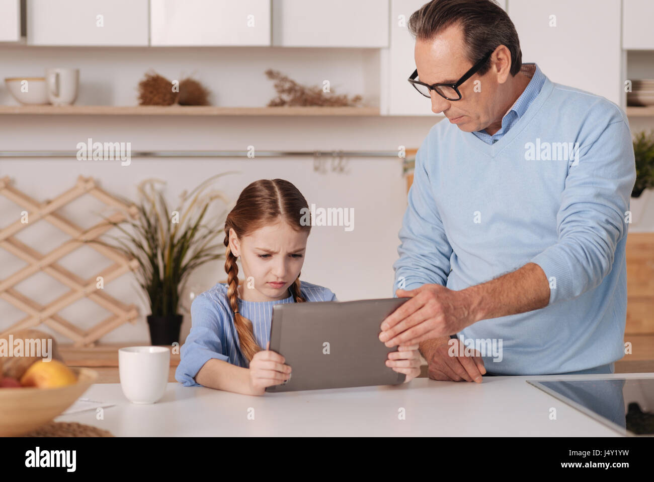 Aged man taking away tablet from little granddaughter indoors Stock ...