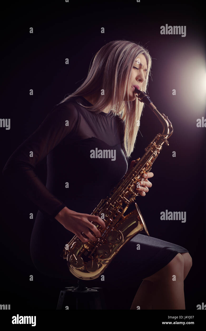 Female jazz musician sitting on a chair and playing a saxophone during ...