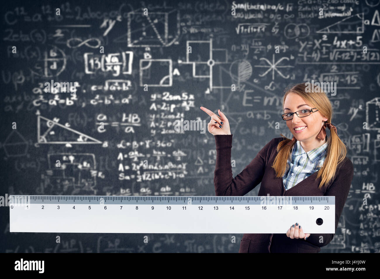 female smiling student with a big ruler pointing formulas on background ...