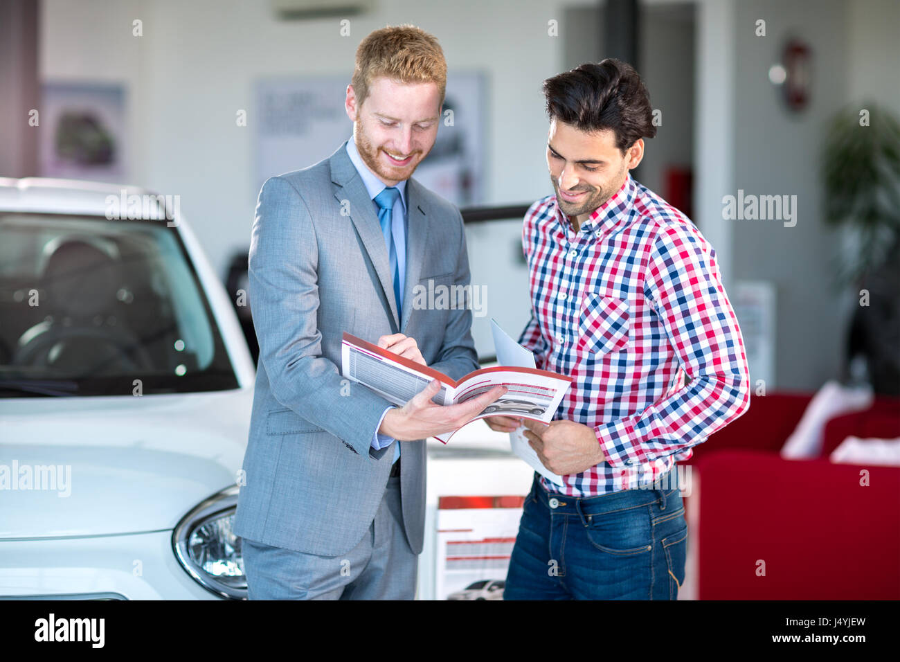 Male Caucasian salesman and male client at the car dealership saloon ...
