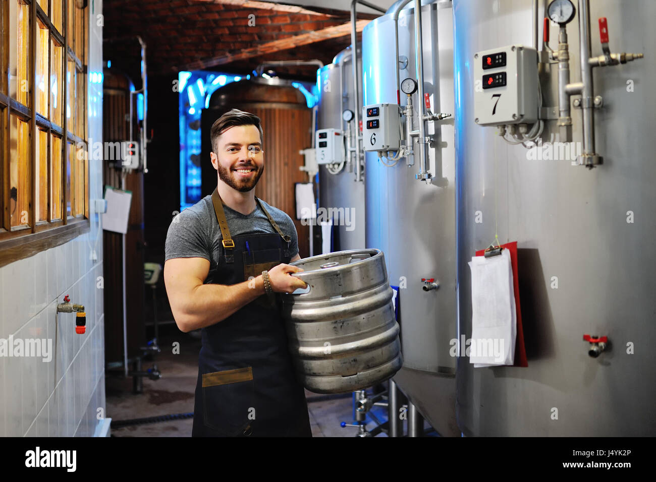 Man with a beard working in uniform with a barrel of beer in a brewery ...
