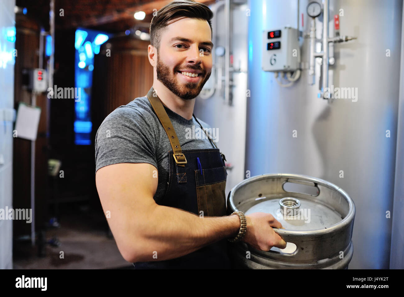 Male brewer with a metal beer barrel on the background of the brewery ...