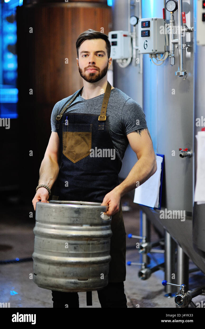 Male brewer with a metal beer barrel on the background of the brewery ...