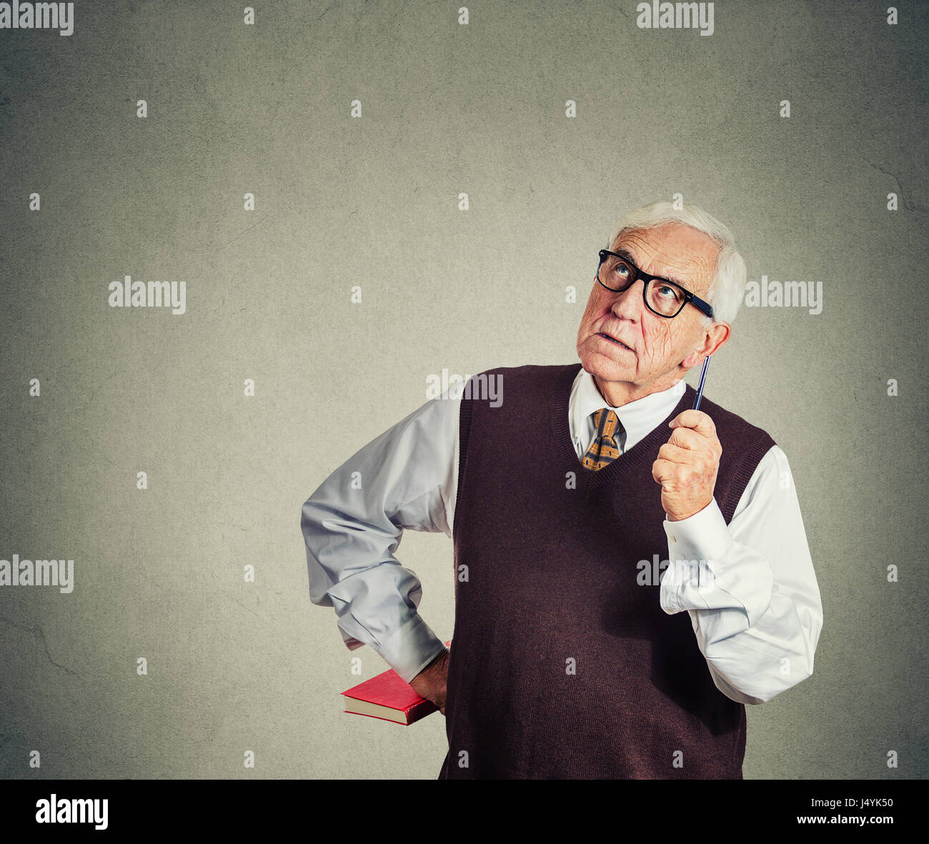 Closeup portrait senior strict teacher holding book and pen, looking up ...