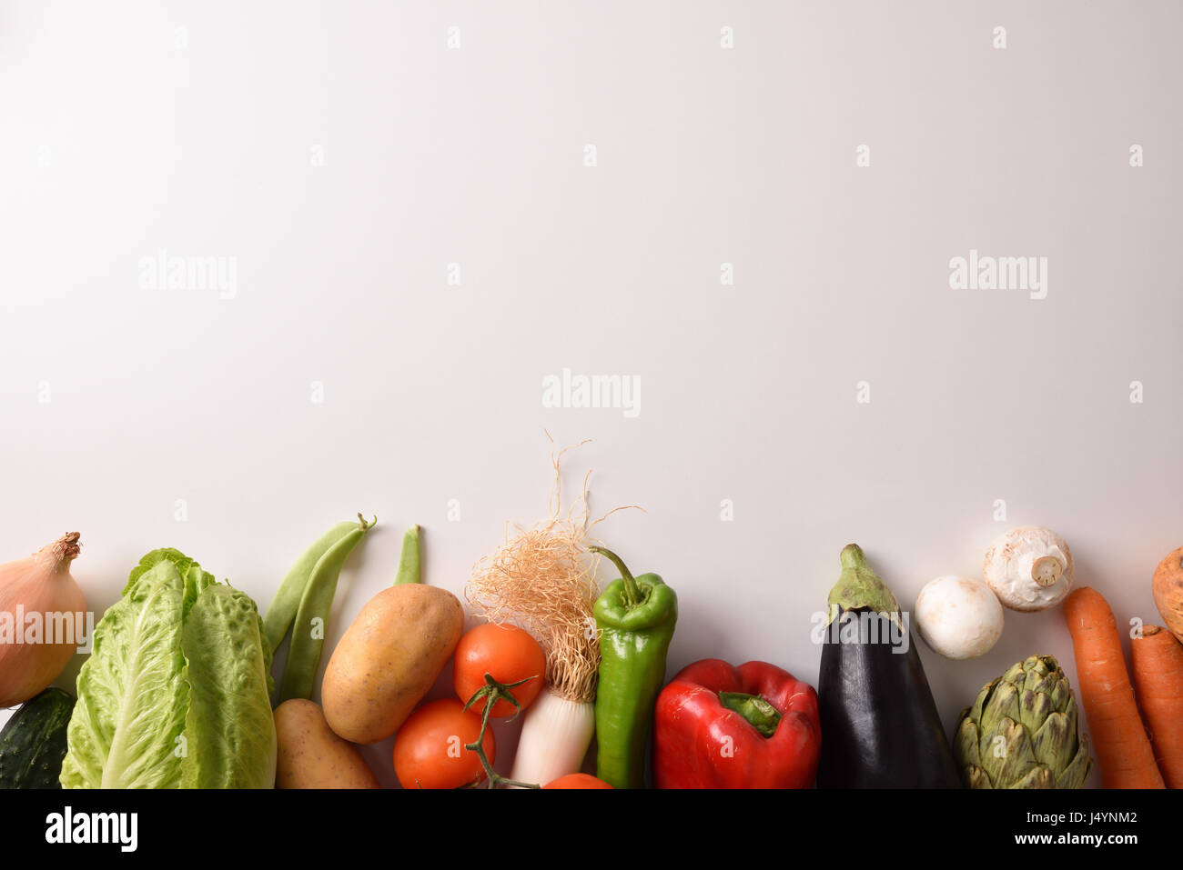 Assortment of vegetables lined up on a white table. Horizontal ...